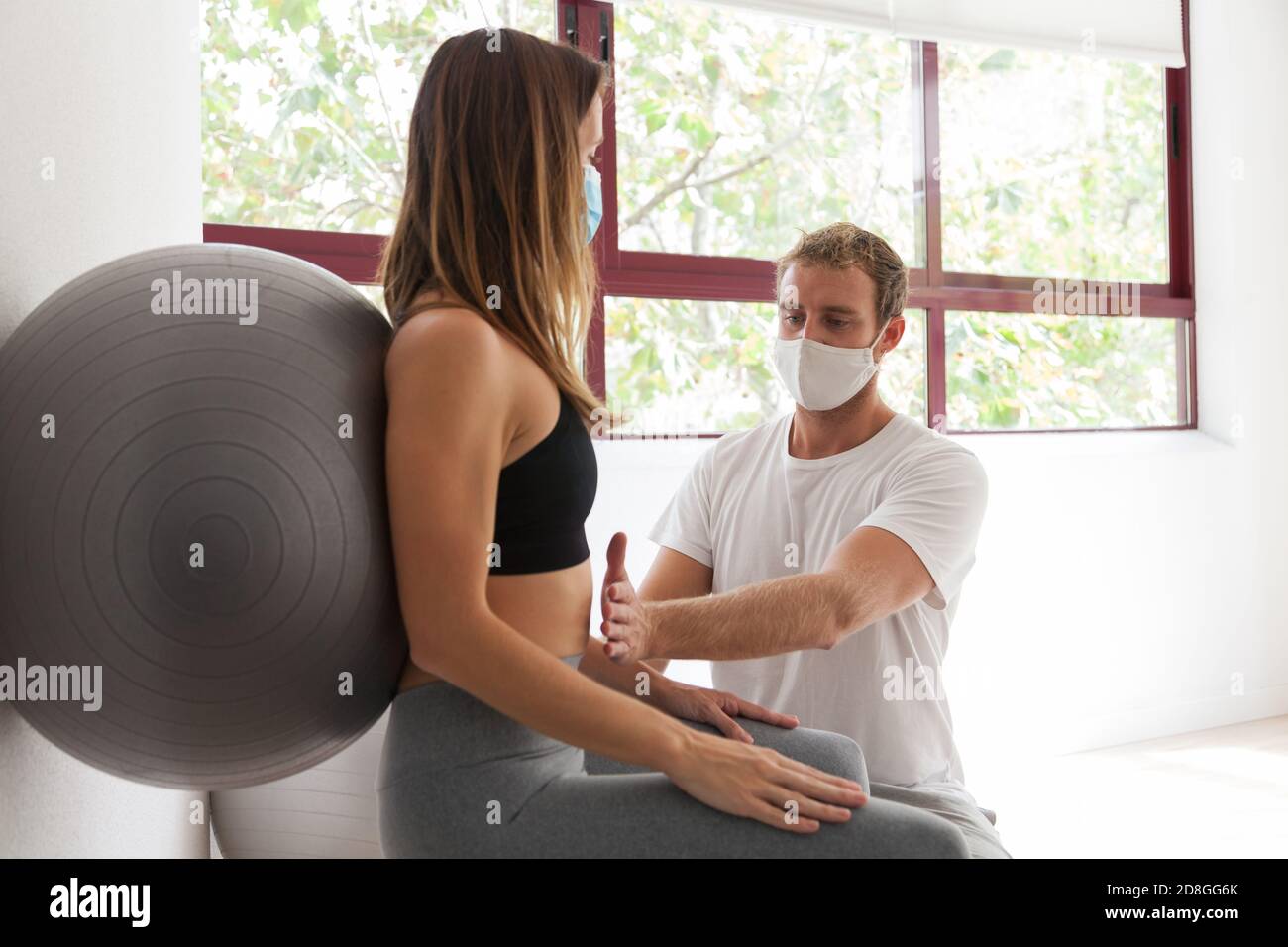 Young woman doing fitness ball and pilates exercise with coach wearing ...