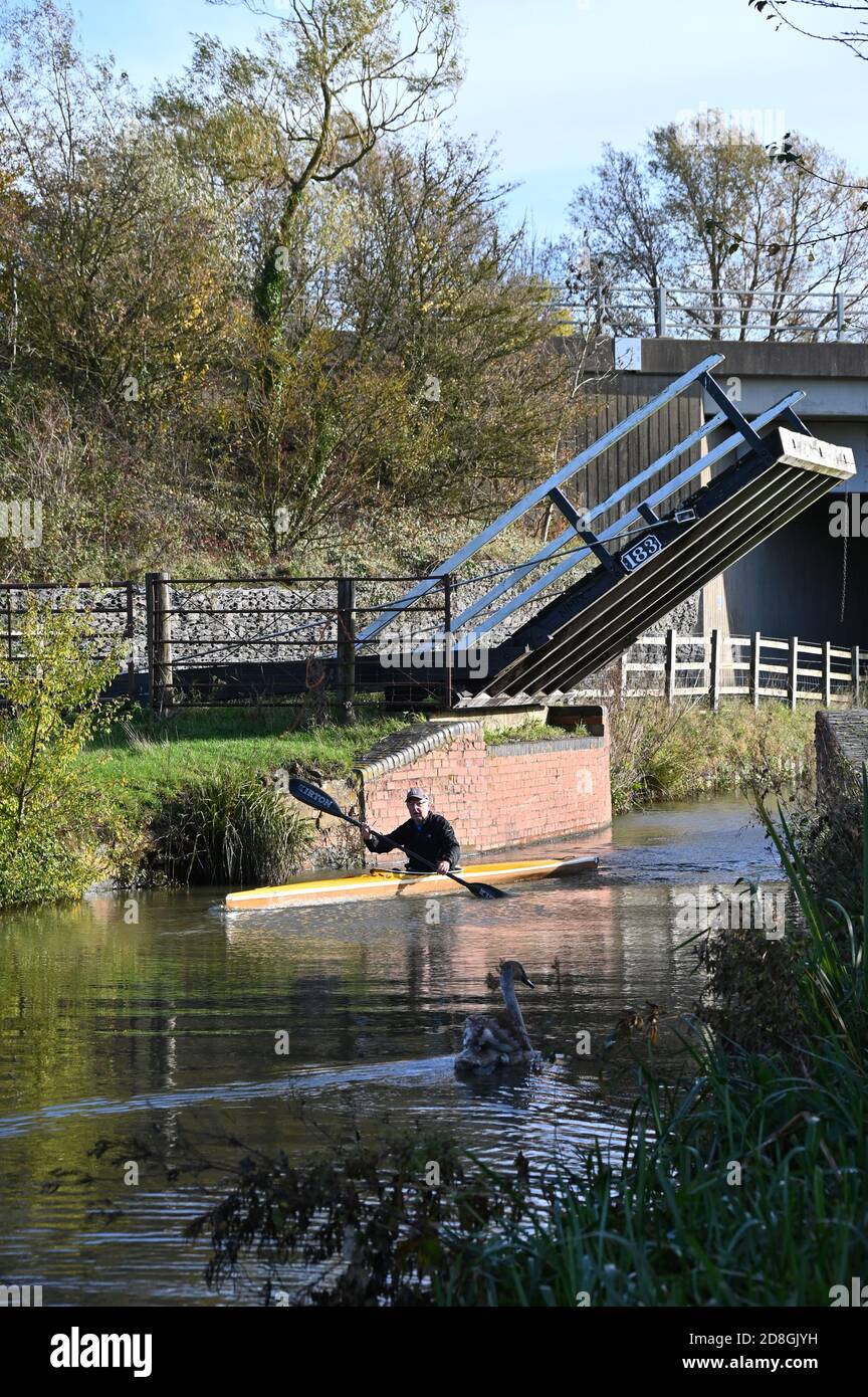 A solo canoeist passes under a raised bridge on rhe Oxford Canal near ...
