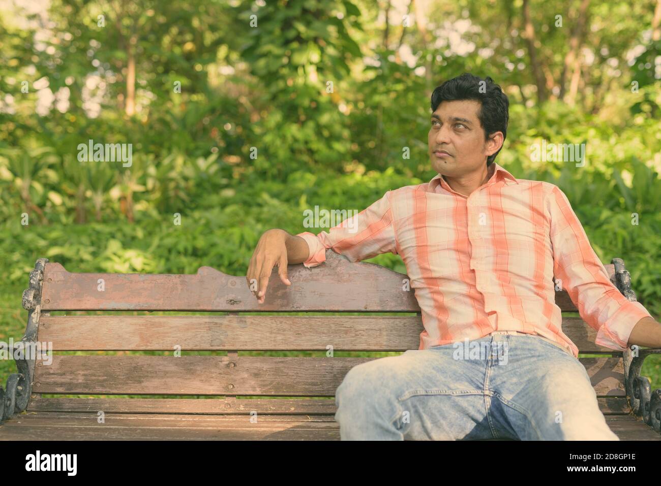 Indian man thinking while sitting on wooden bench in peaceful green ...