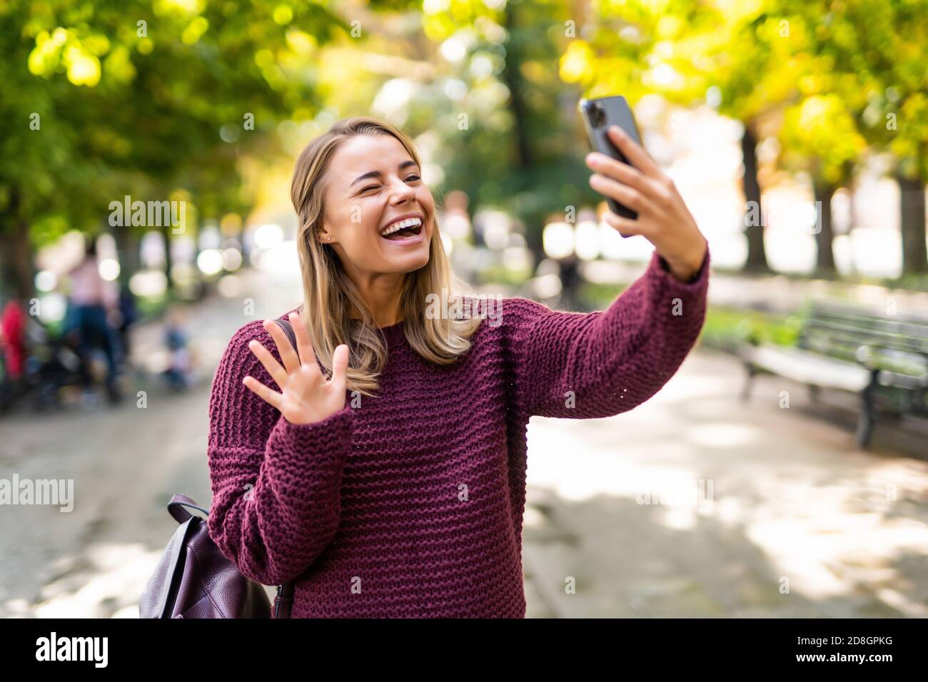 Happy girl waving hand greeting during a phone video call in the street ...