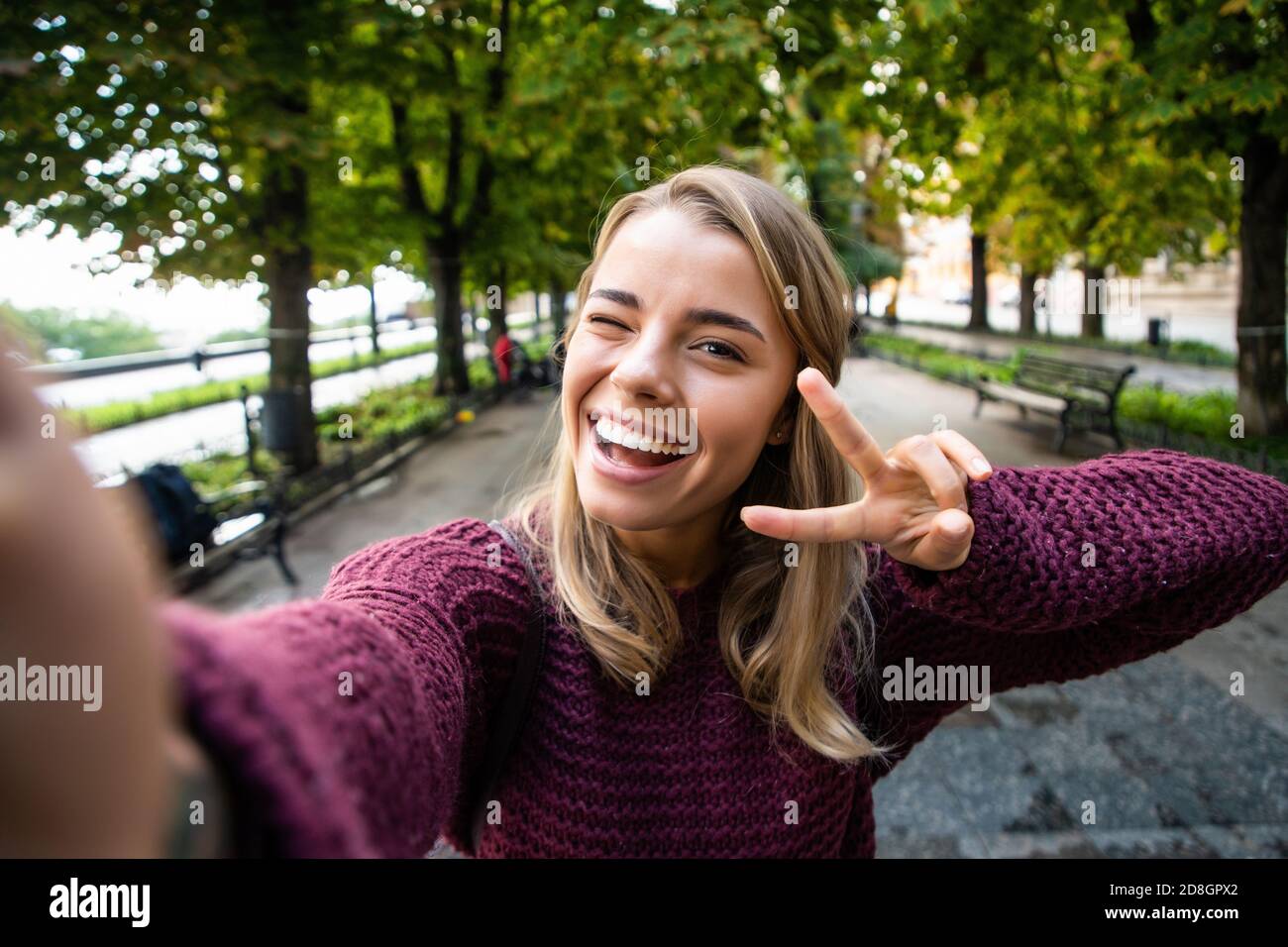 young attractive cheerful girl takes a selfie and makes peace sign with ...
