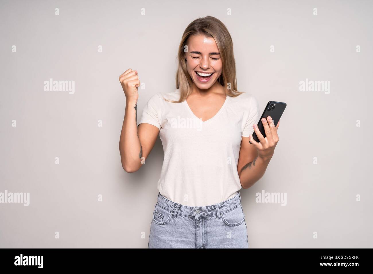 Portrait of a happy joyful girl holding mobile phone and celebrating a ...