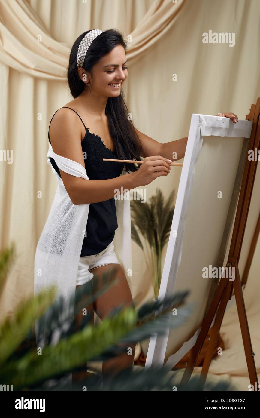 Young happy female artist in front of easel. Woman painting in art ...