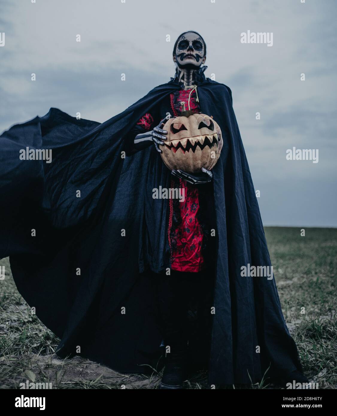 Young woman stands among field in Halloween costume of death with ...