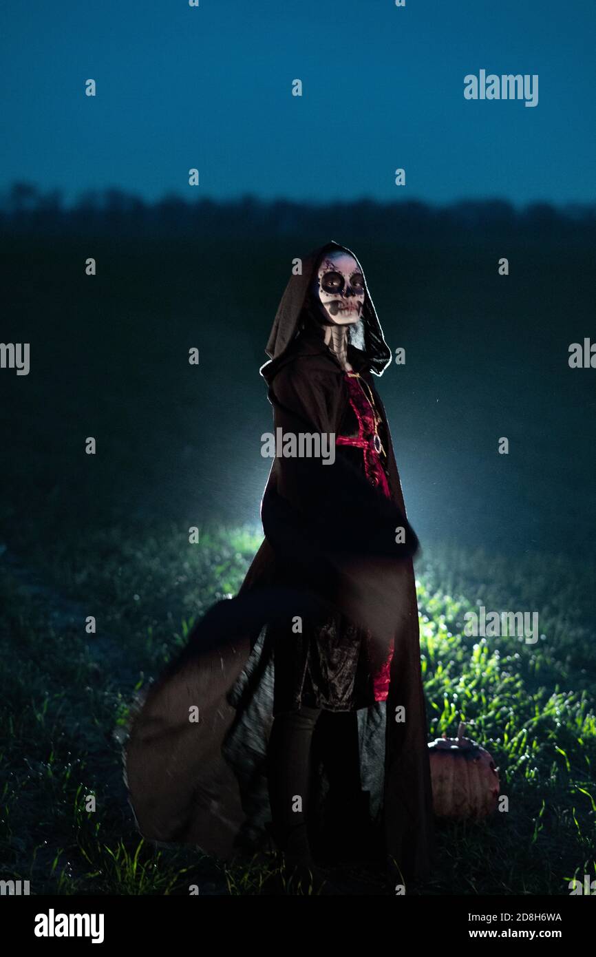 Young woman stands among field in Halloween costume of death with ...