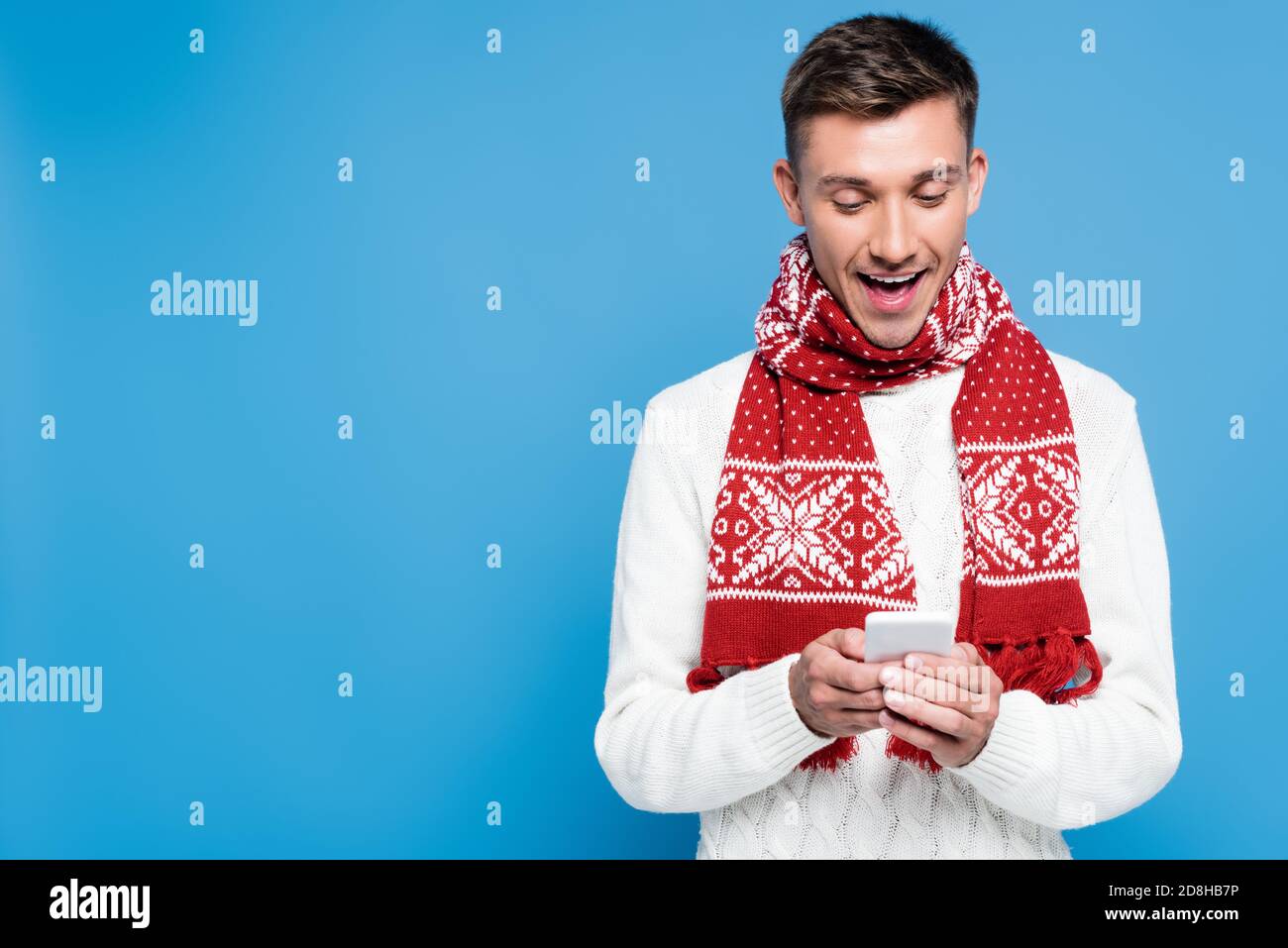 Excited man wearing knitted scarf and sweater, texting on smartphone ...