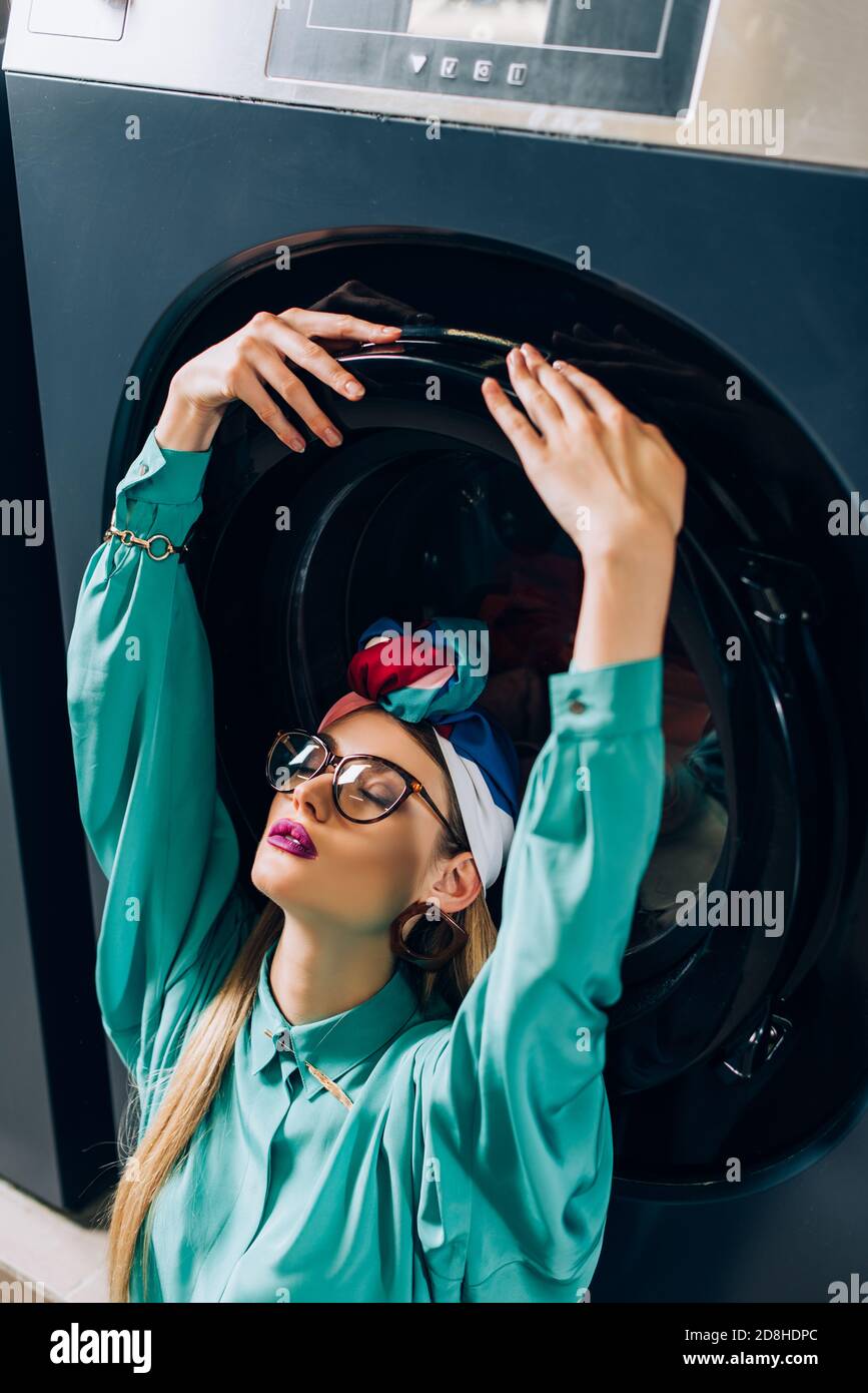 stylish young woman in glasses and turban touching door of washing ...