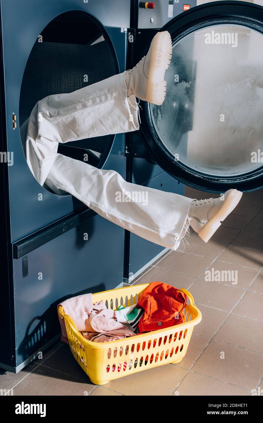 legs of woman sticking out of washing machine near basket with dirty ...