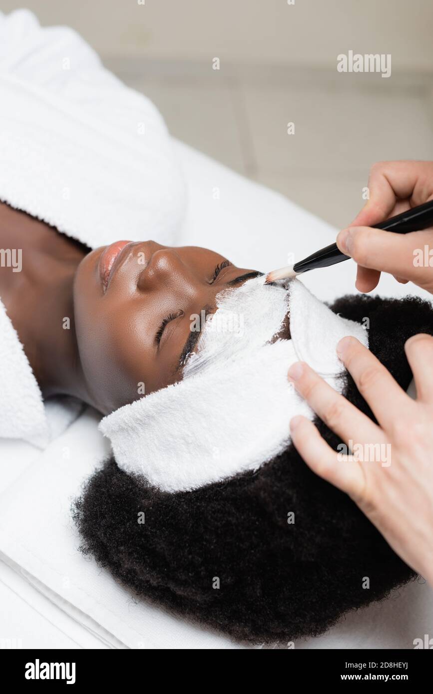 Overhead view of spa therapist applying face mask with cosmetic brush ...