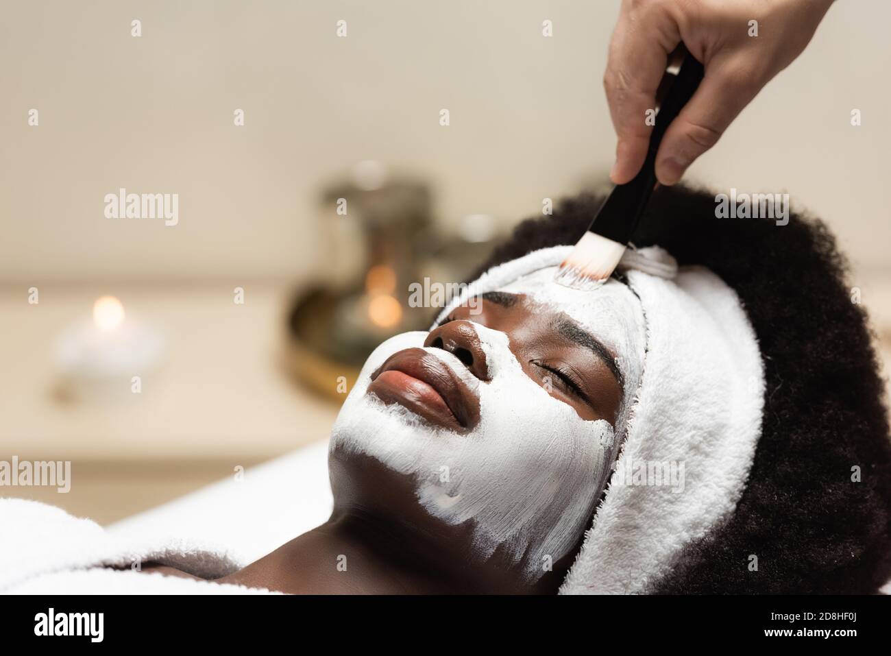 African american woman in headband lying near spa therapist applying ...