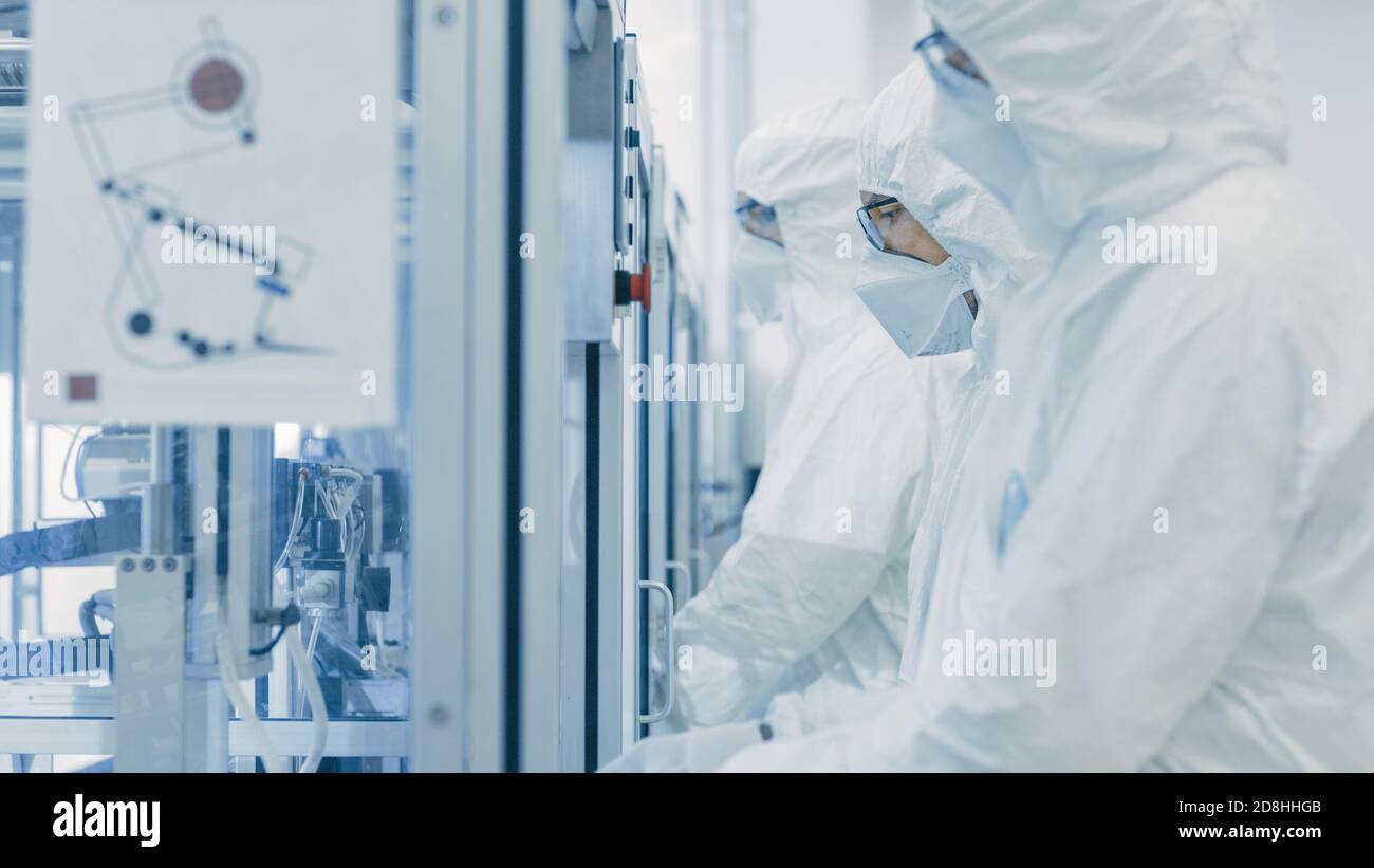 On a Factory Team of Scientists in Sterile Protective Clothing Work on ...