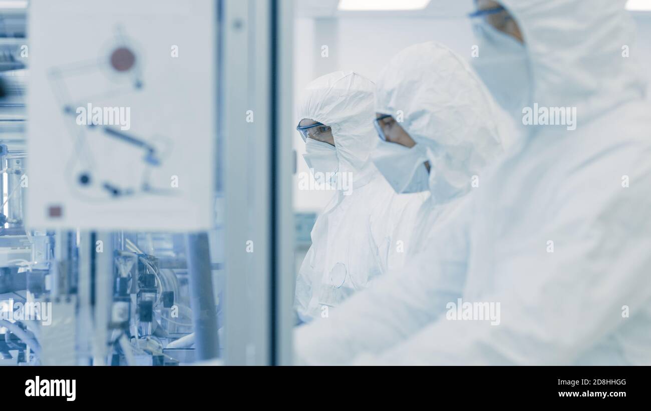 On a Factory Team of Scientists in Sterile Protective Clothing Work on ...