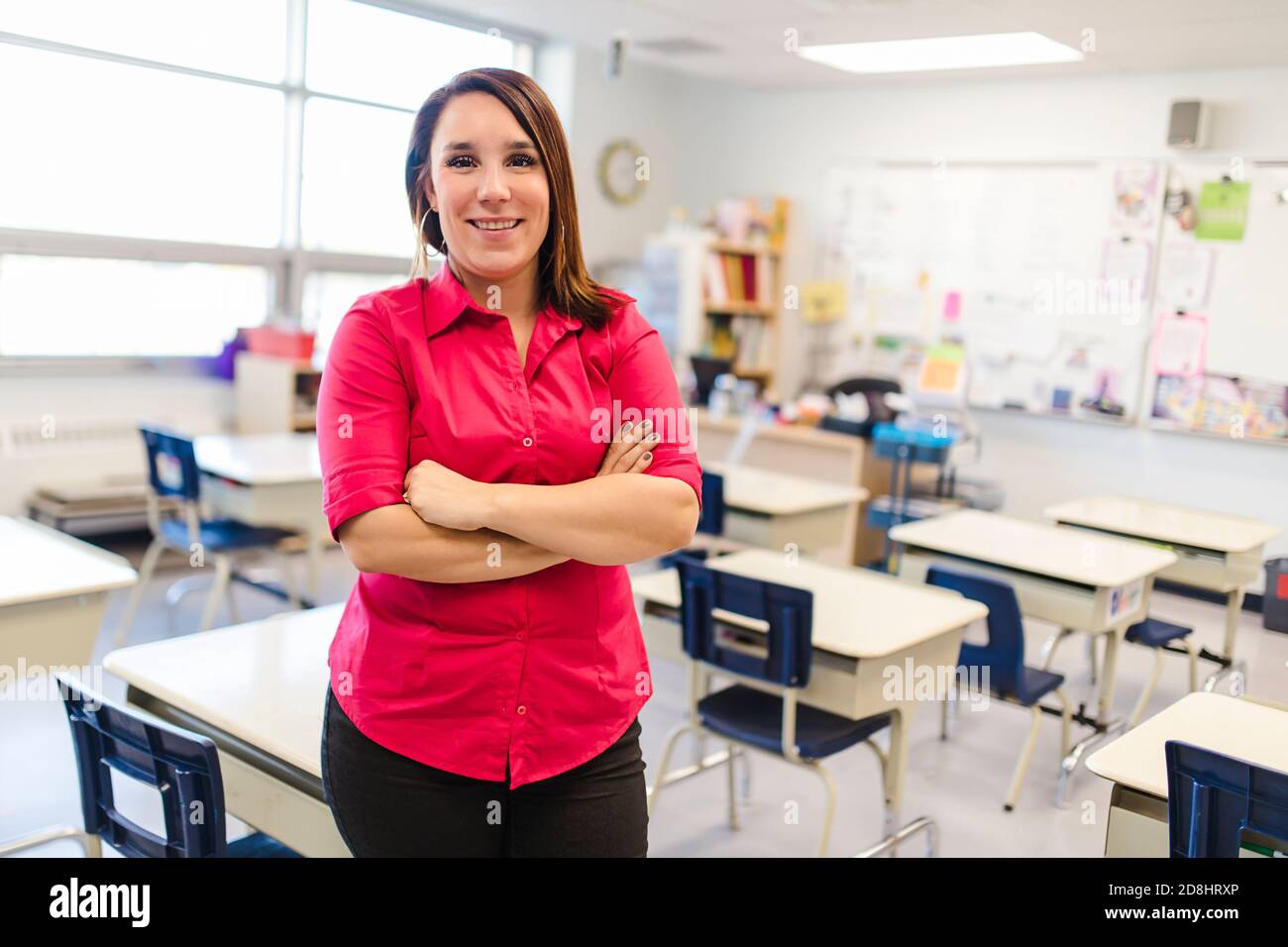 A Pretty teacher smiling at camera at back of classroom at the ...