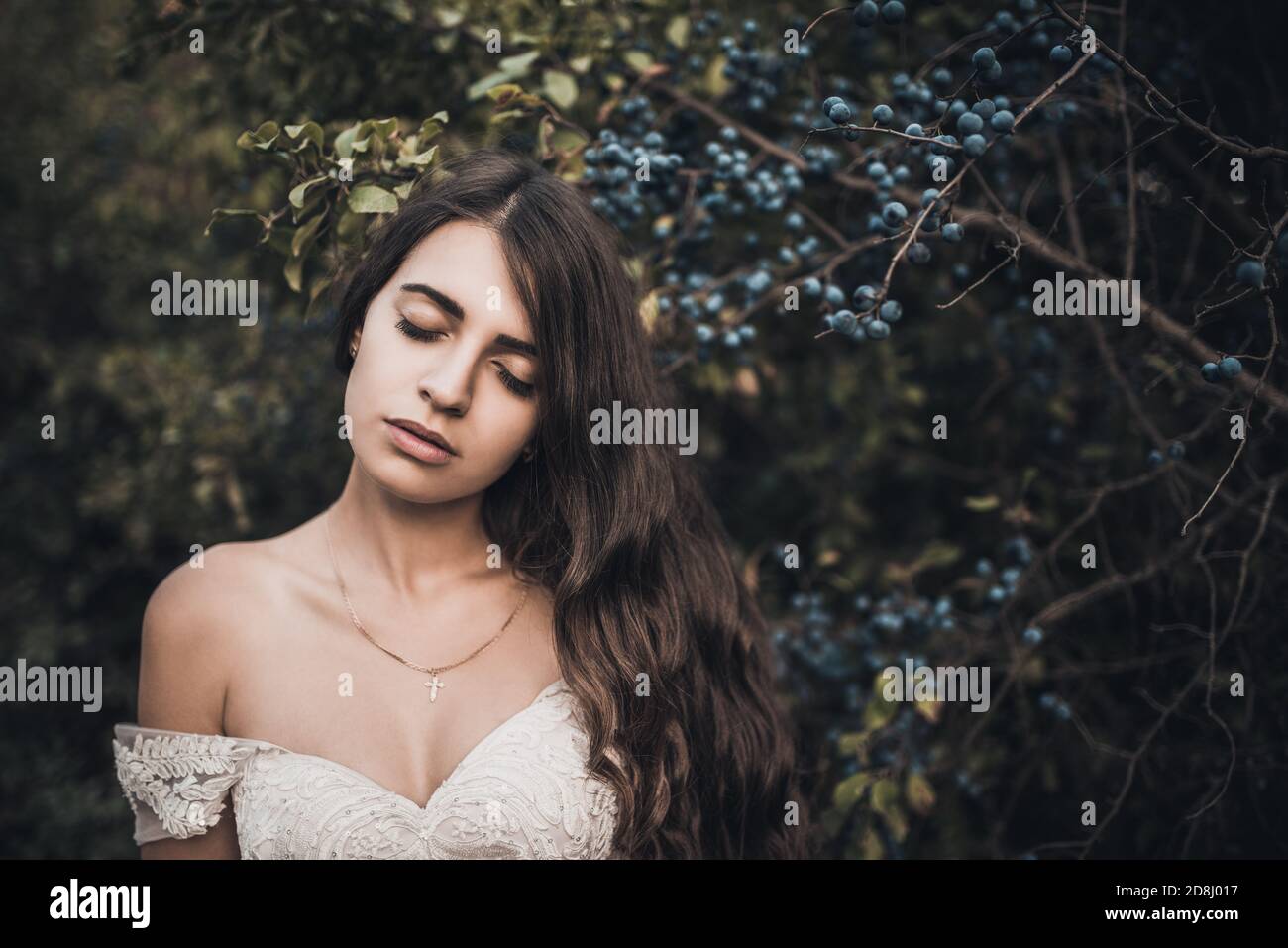 Woman Long-haired bride with bare shoulders near green bush blueberries ...