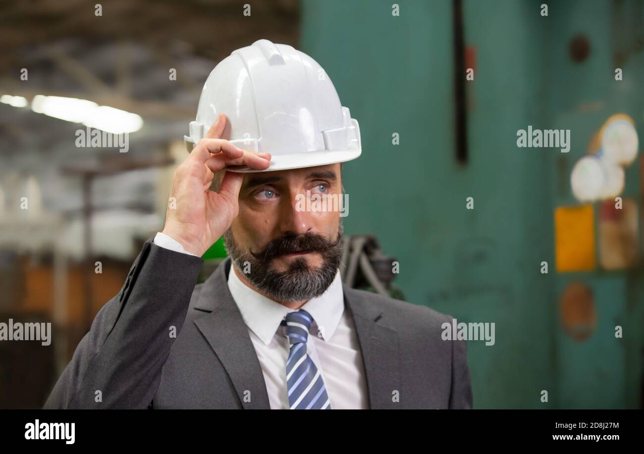 The bearded hipster director with engineer hat standing against machine ...