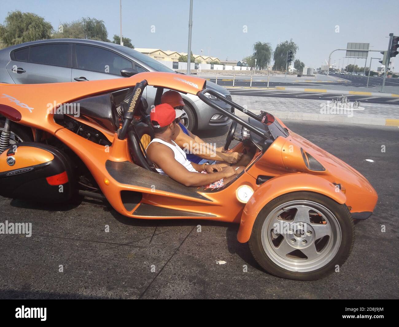 Two muscly guys drive open fancy orange car at the roads of Abu Dhabi ...