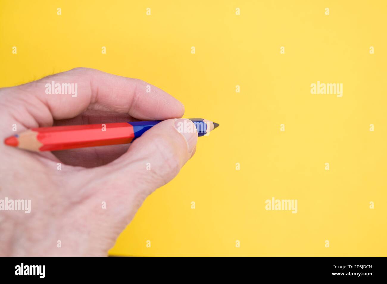 Hand holding a red and blue split pencil on yellow background for a ...