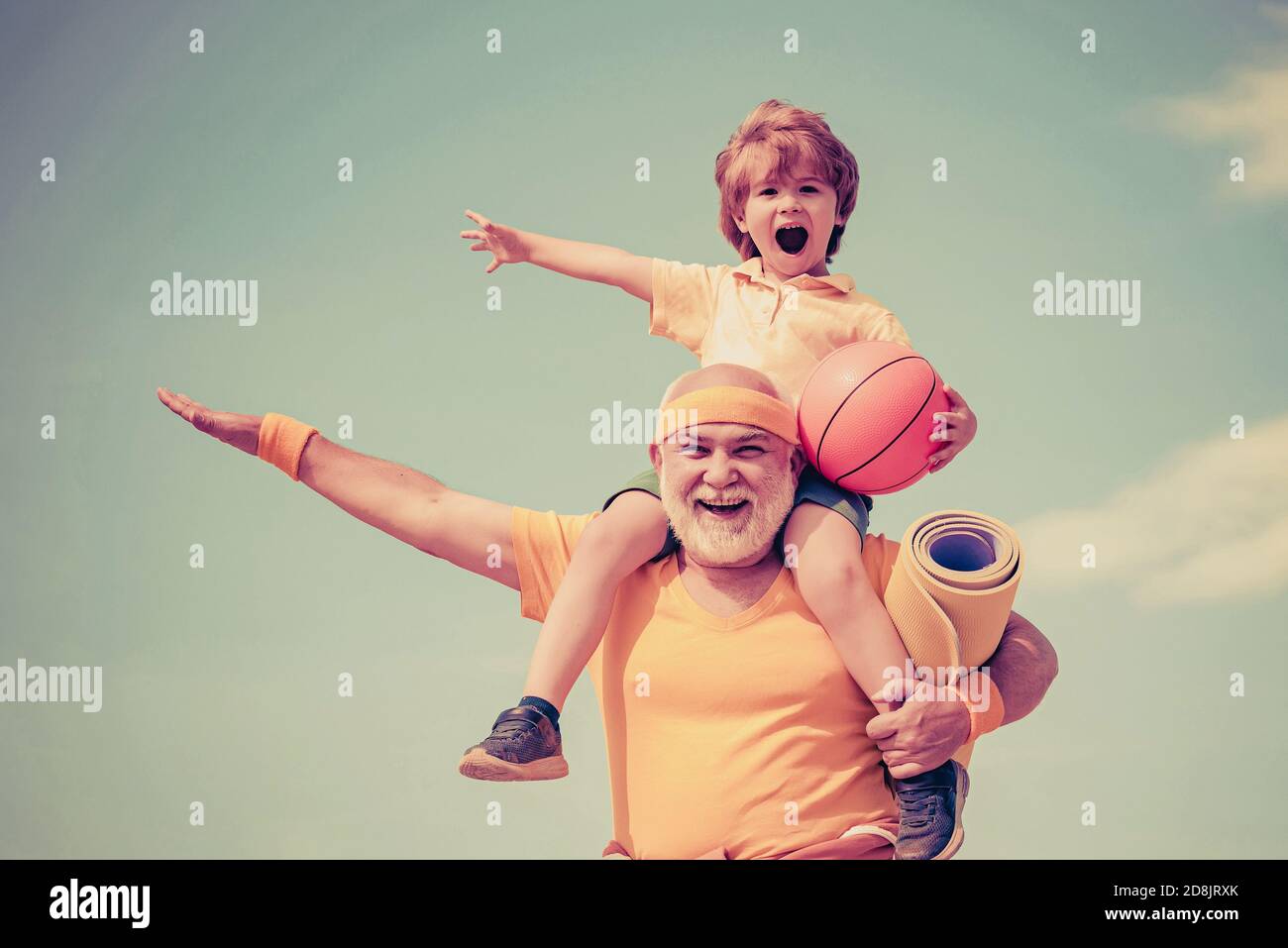 Sportsman grandfather and healthy kid with basketball ball on blue sky ...