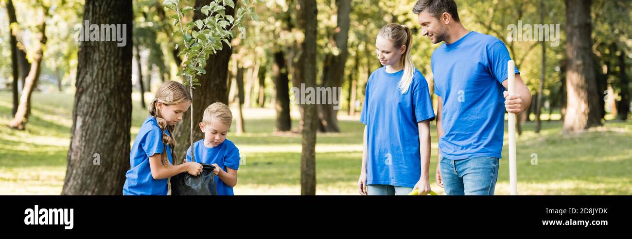 children carrying young tree near parents in forest, ecology concept ...
