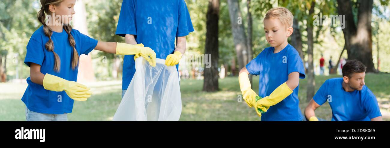 family of volunteers in rubber gloves collecting garbage in recycled ...
