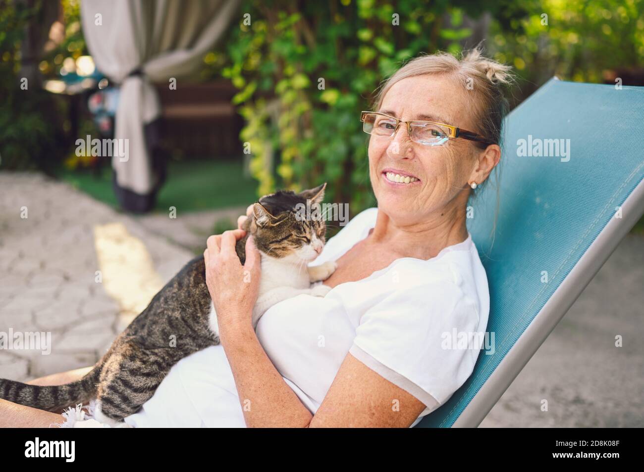Happy smiling senior elderly woman in glasses relaxing in summer garden ...