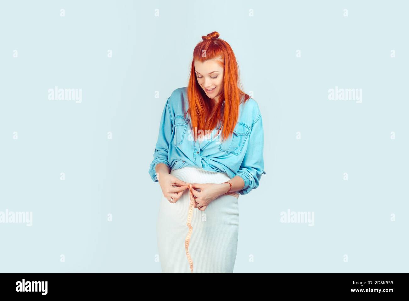 Charming casual woman with baby in belly measuring tummy happily with ...