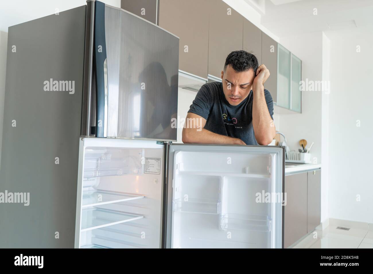The guy is sad near the empty refrigerator without food. Food delivery ...
