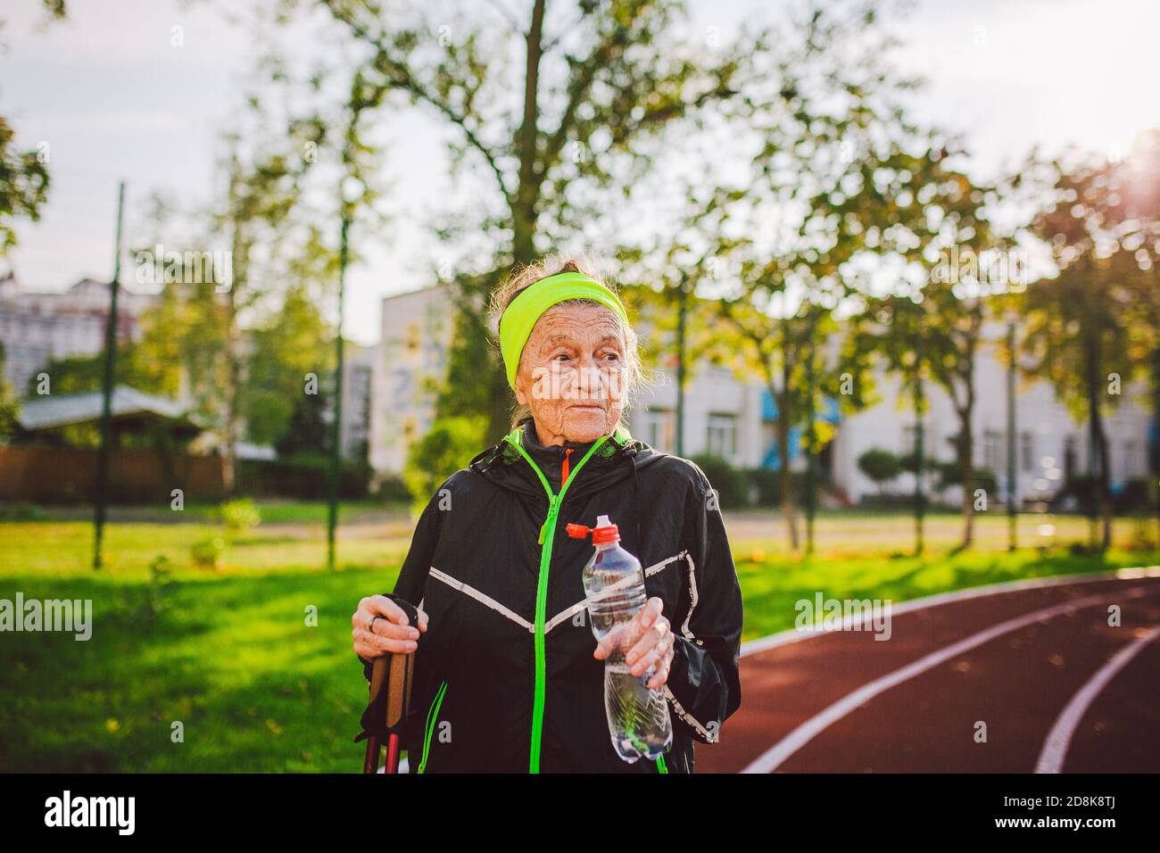 Old woman walking with nordic walk sticks on running track, rubber ...