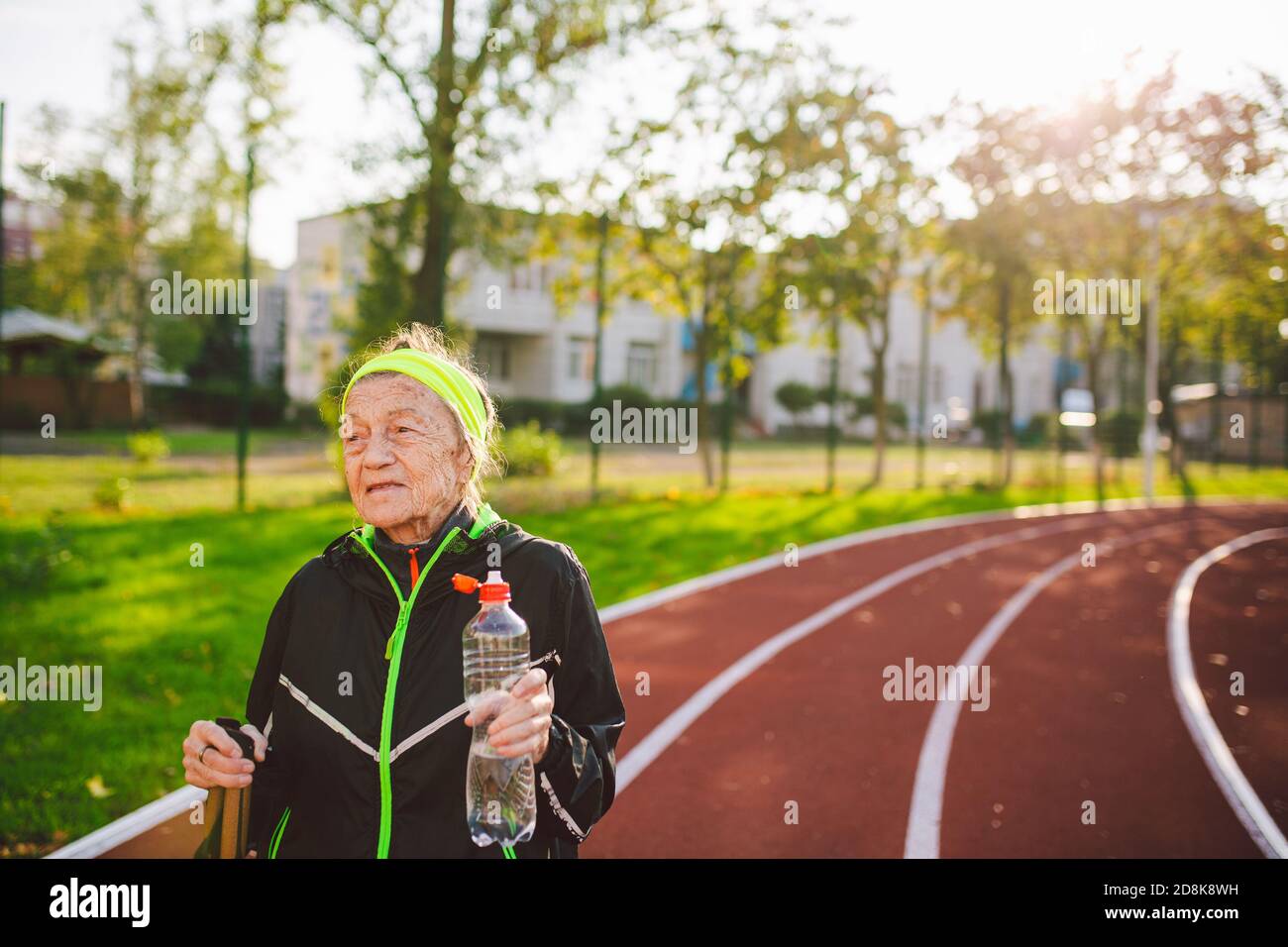 Old woman walking with nordic walk sticks on running track, rubber ...