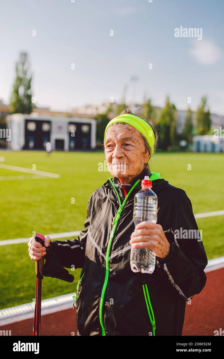 Old woman walking with nordic walk sticks on running track, rubber ...