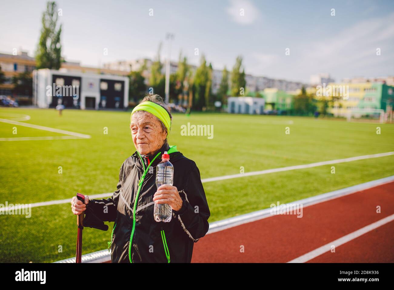 Old woman walking with nordic walk sticks on running track, rubber ...