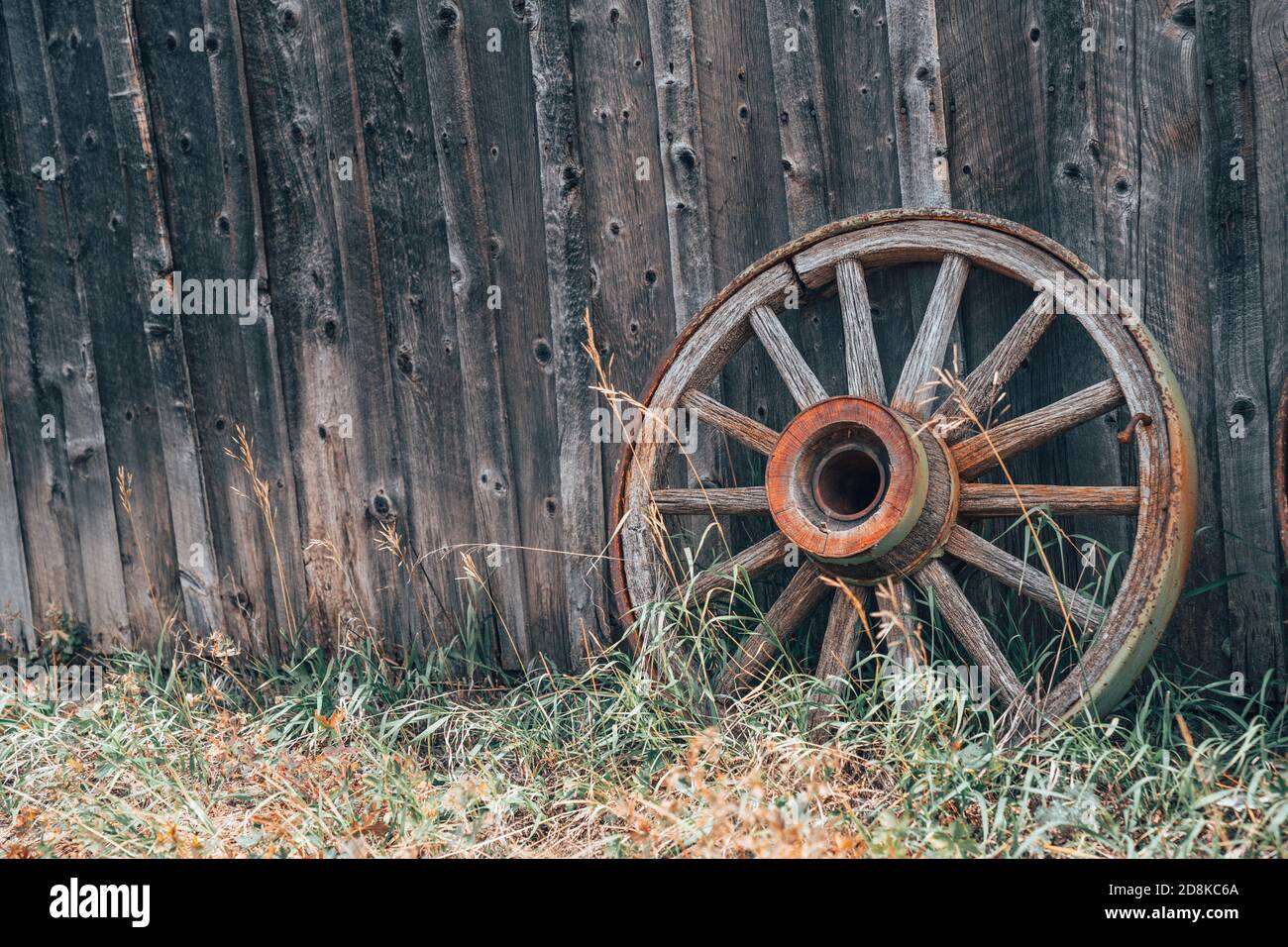 One rusty wagon wheels against a wooden wall, with grass. Useful for ...