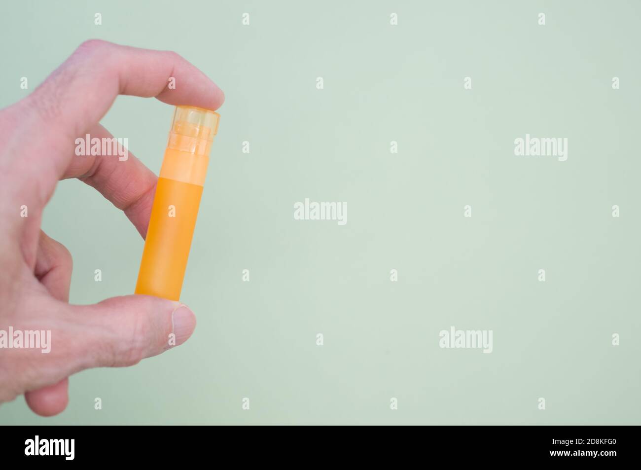 Hand holding an empty small orange plastic tube on pastel green ...