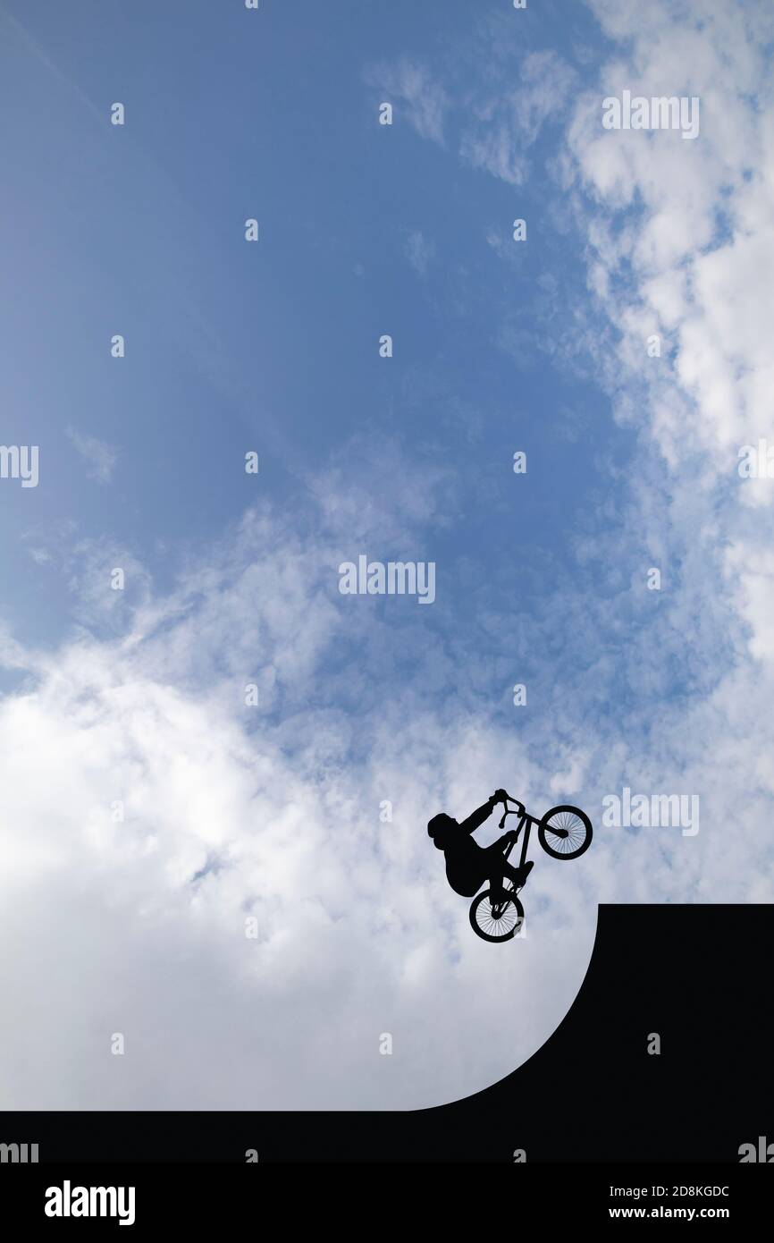 Silhouetted BMX rider performing stunts set against a blue cloudy ...