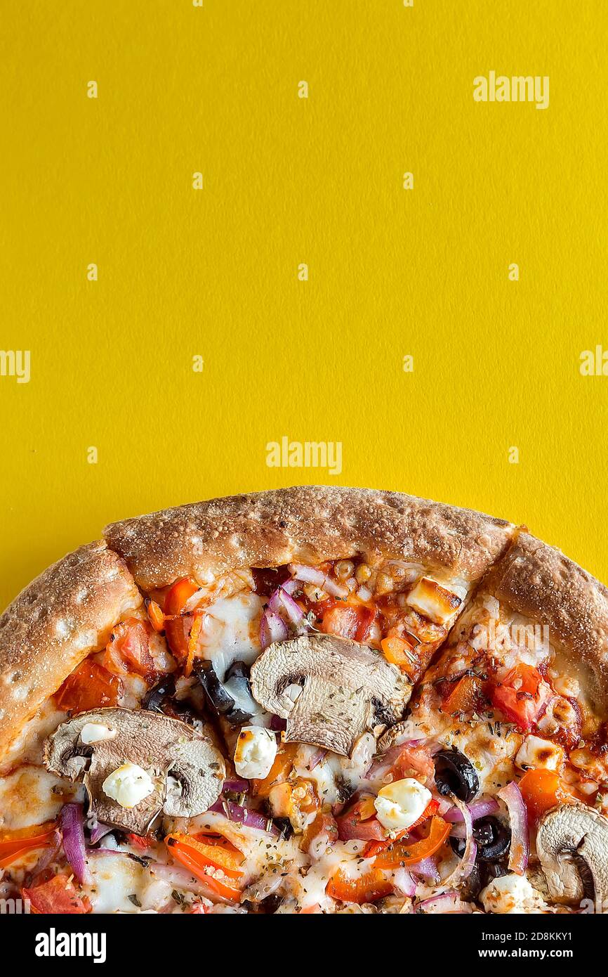 Half A pizza with vegetables is on a bright yellow background. Space ...