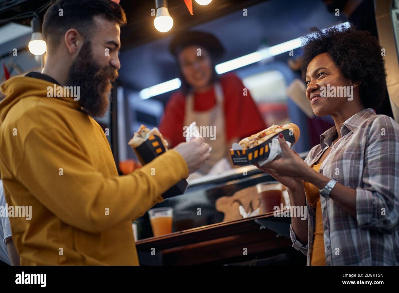 friends talking and smiling while eating sandwiches in front of fast ...