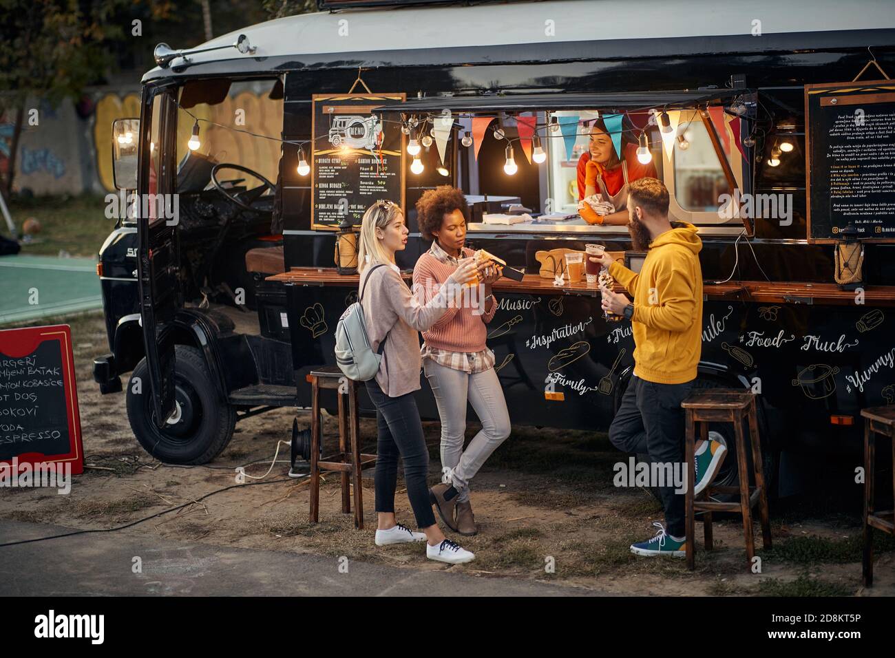 group of young people socializing while eating outdoor in front of ...