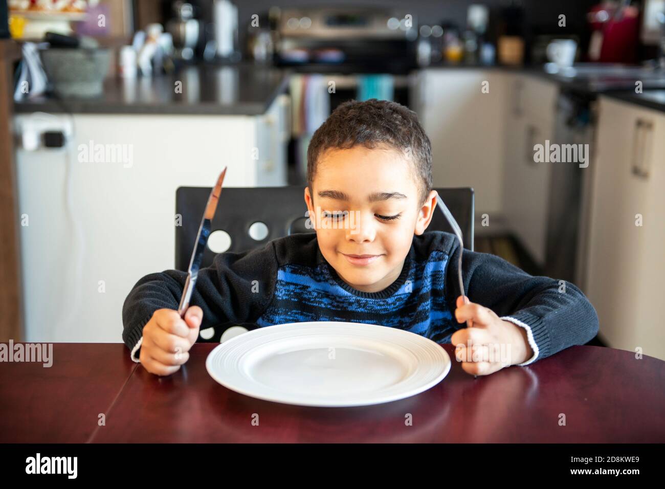 Boy sitting at the kitchen table with empty plate Stock Photo - Alamy