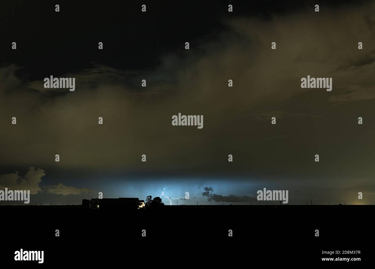 Thundercloud with lightning bolt hitting the earth behind a farm in the ...