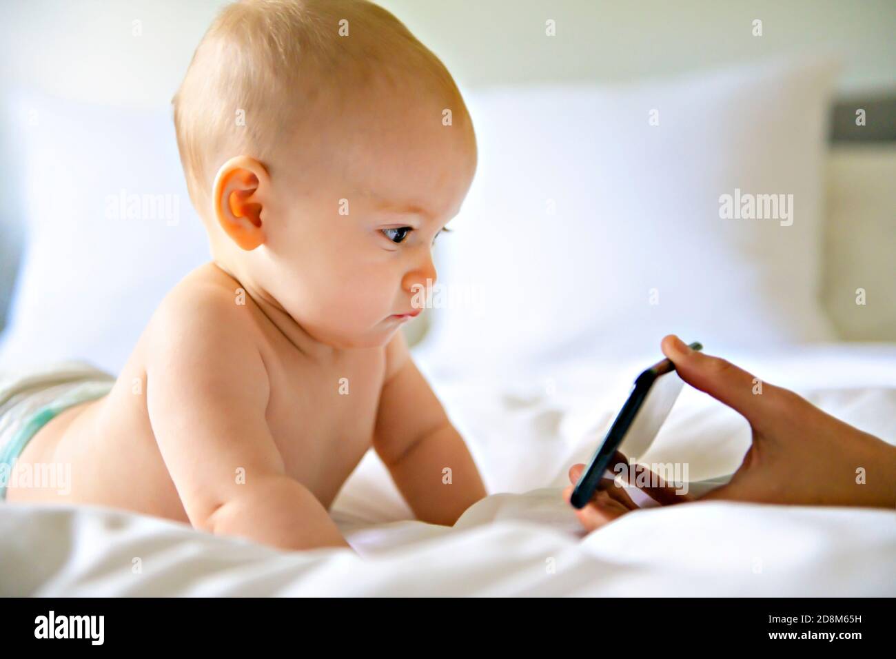 A portrait of a cute baby checking smartphone lying in a bed Stock ...