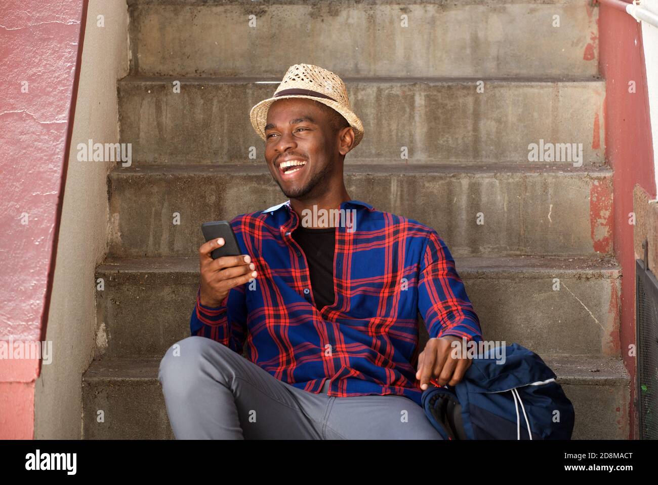 Portrait of happy african american man relaxing on steps with backpack ...