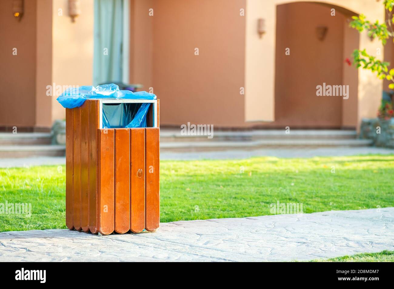 Yellow wooden trash can outdoors on the side of sidewalk in park ...