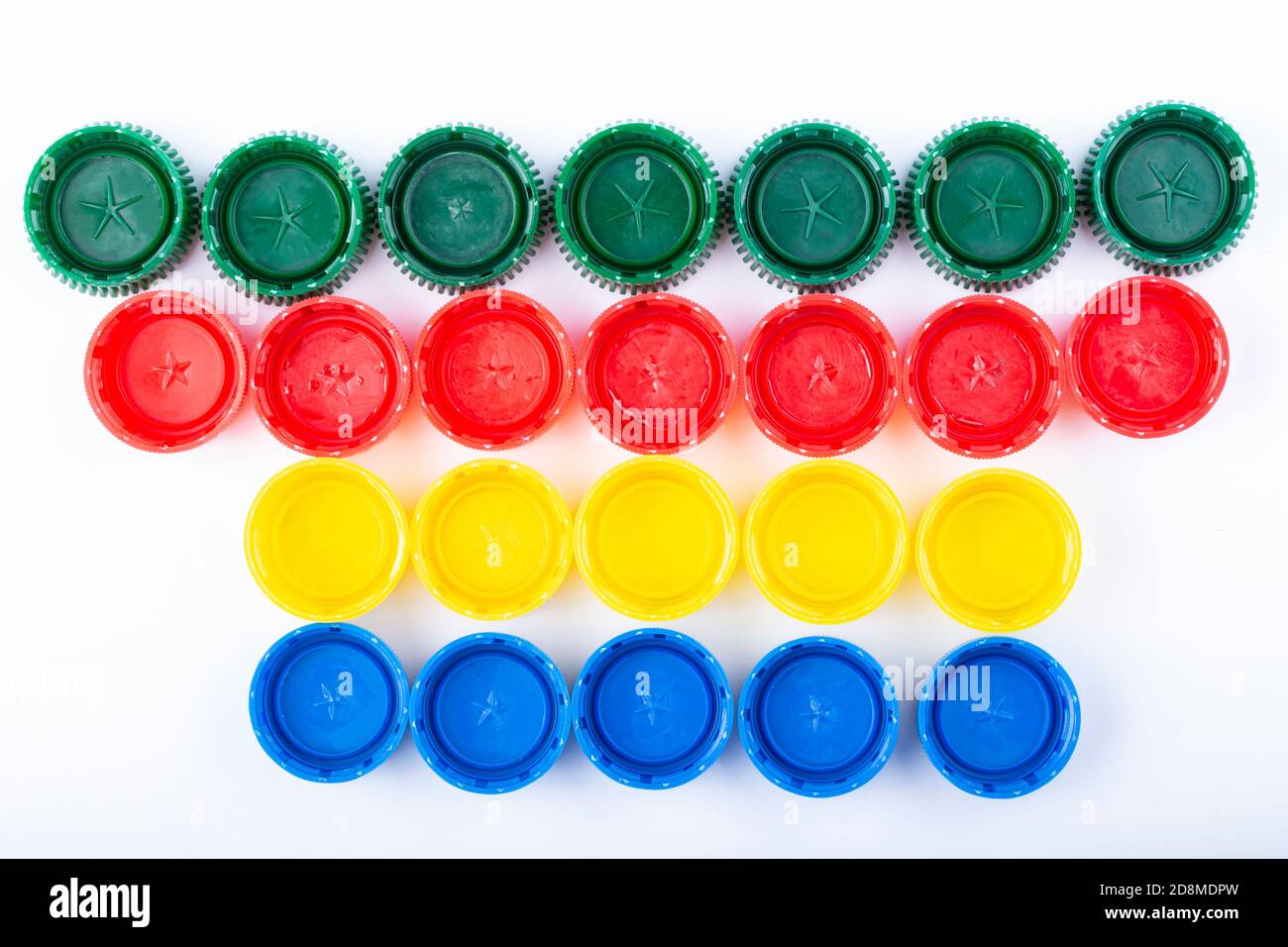 Plastic multi-colored bottle caps are arranged in rows on a white ...
