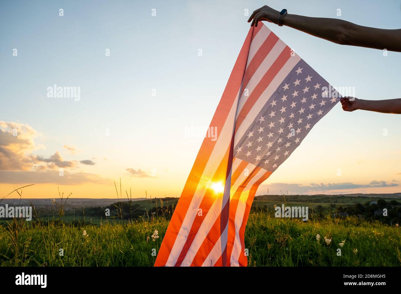 Human hands holding waving american national flag in field at sunset ...