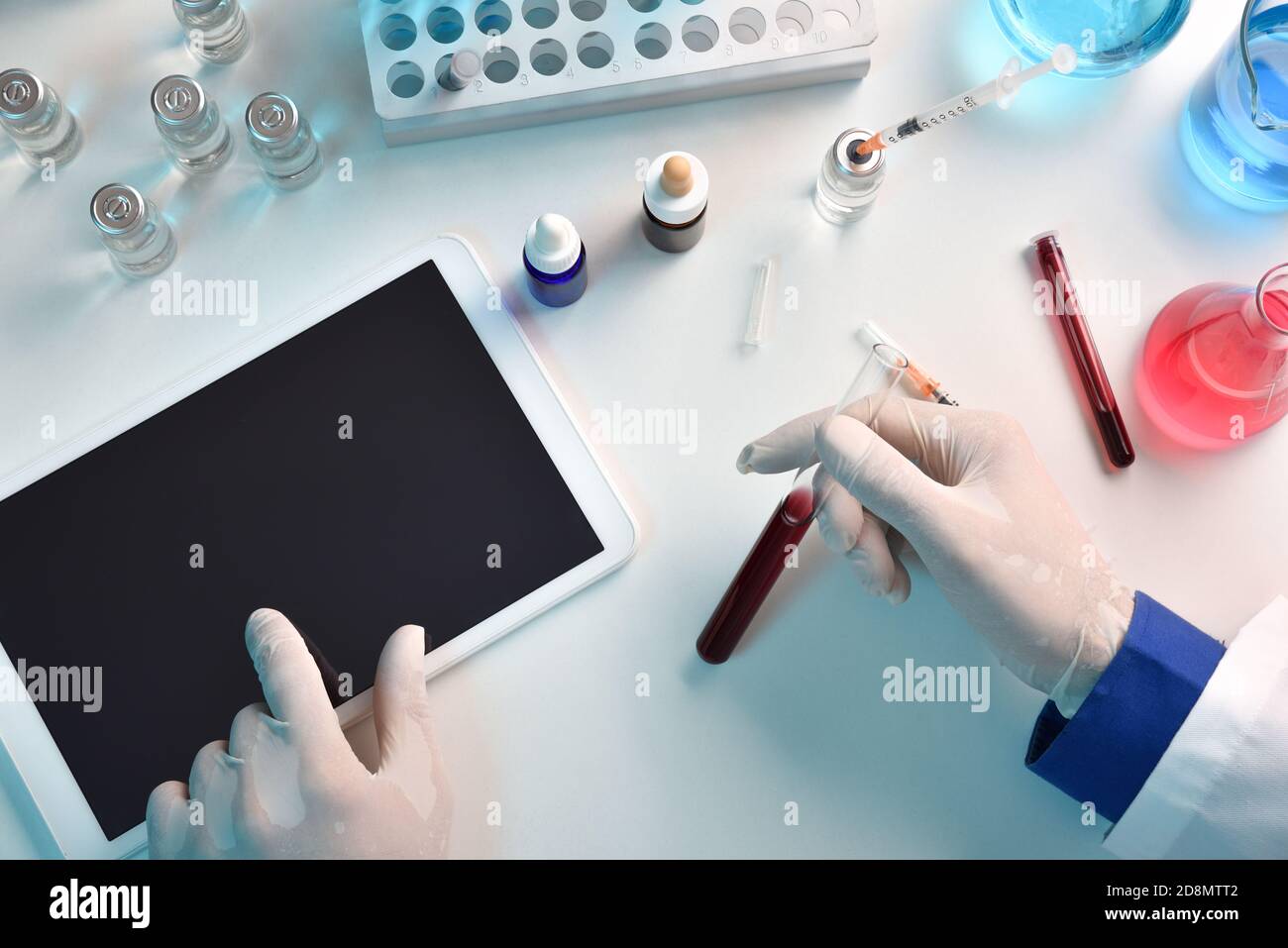 Lab worker using tablet with blood sample on workbench with vials and ...