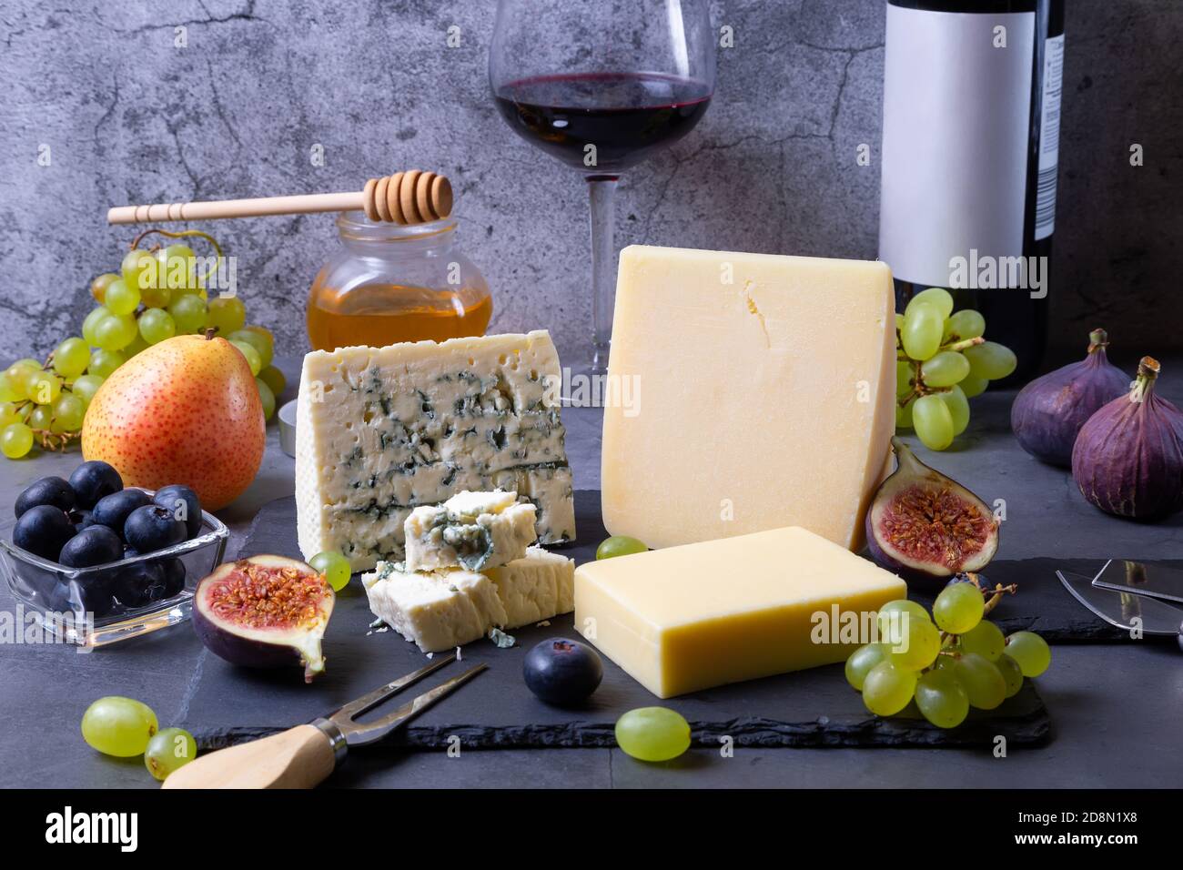 Blue cheese and parmesan on a black board, fruit, wine and honey. Close ...