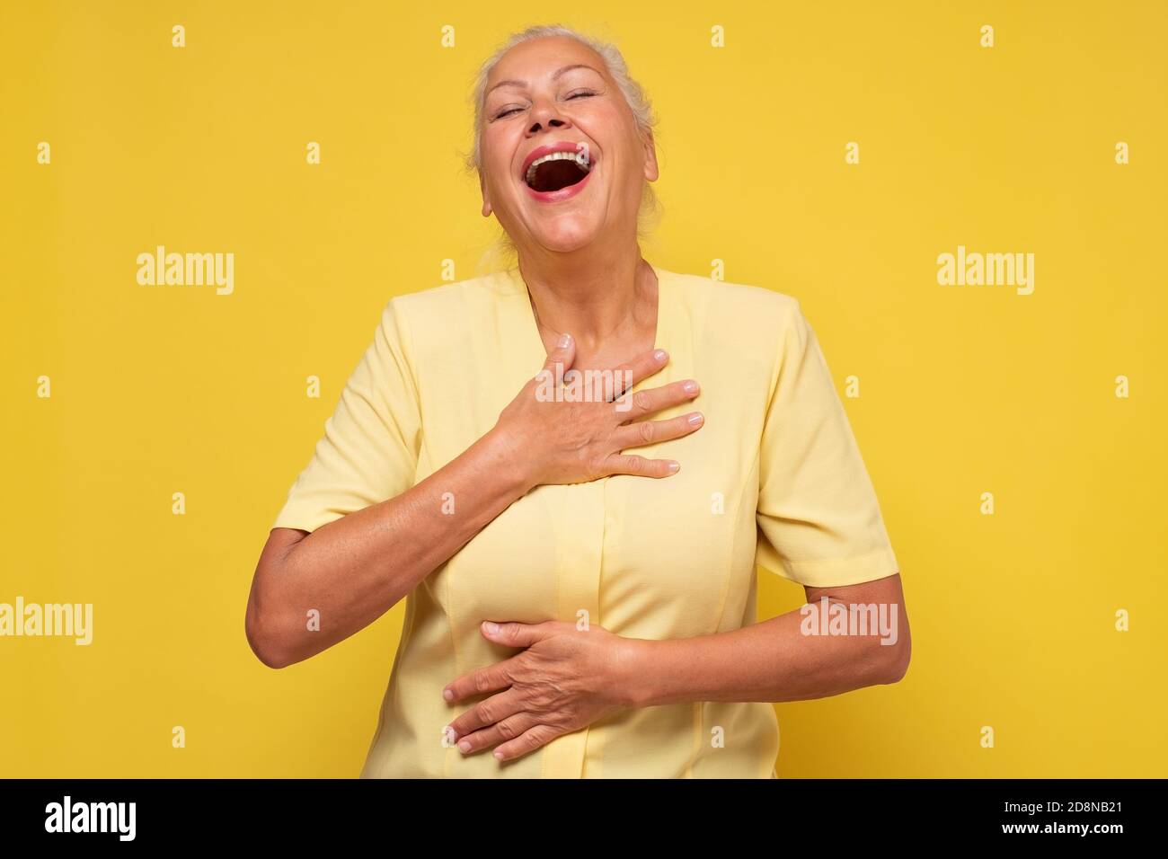 Senior woman smiling happily laughing at the camera on yellow wall ...