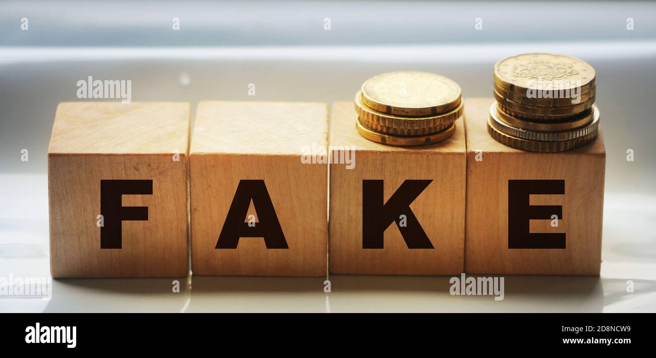 FAKE word written in wooden blocks and stacks of coins. Business and ...