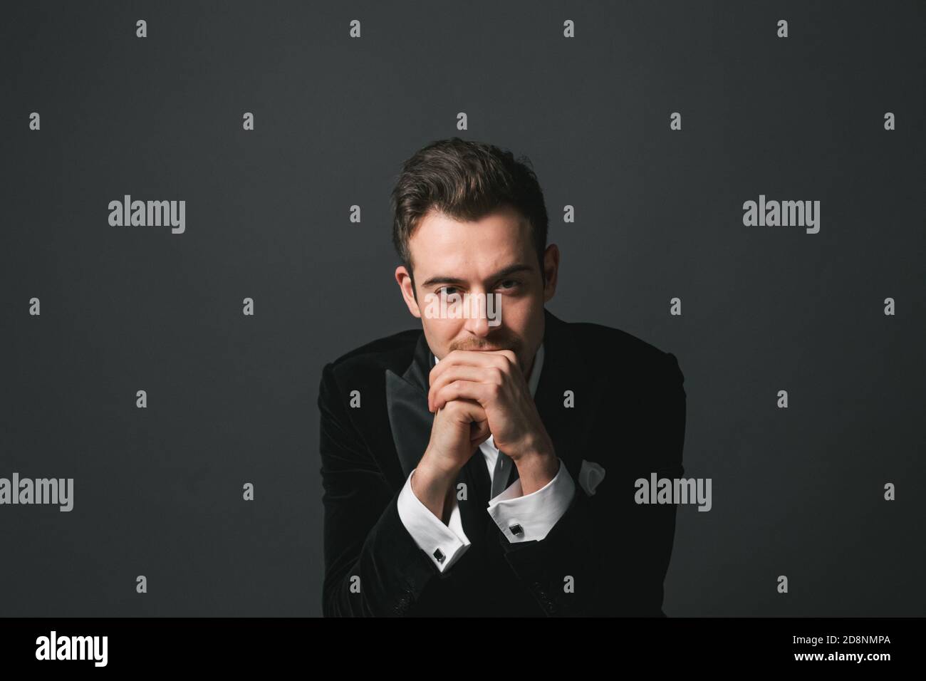 Studio portrait of a young caucasian man in a tuxedo, hands on chin ...