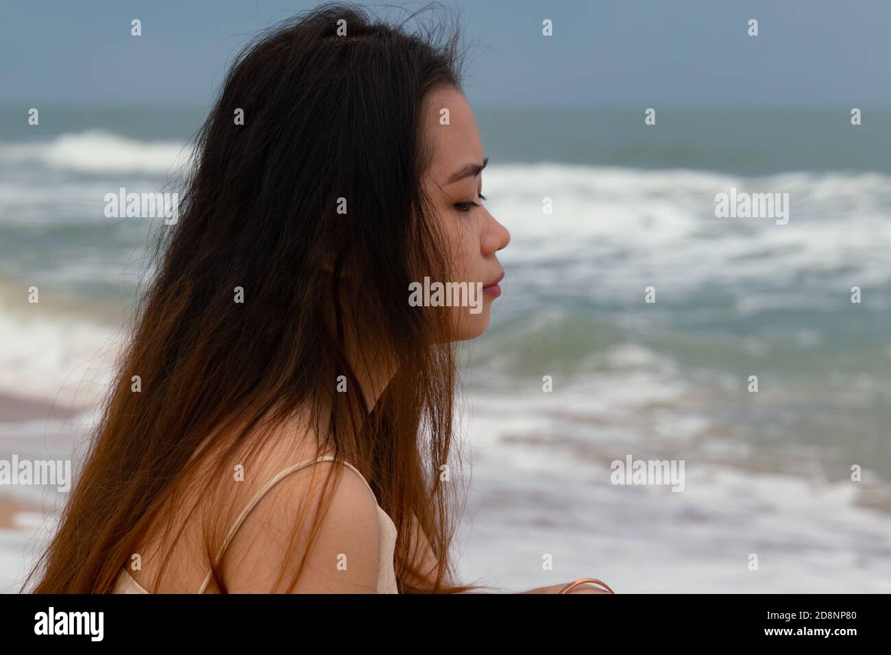Beautiful Asian woman sitting on the sand near the beach and enjoying ...